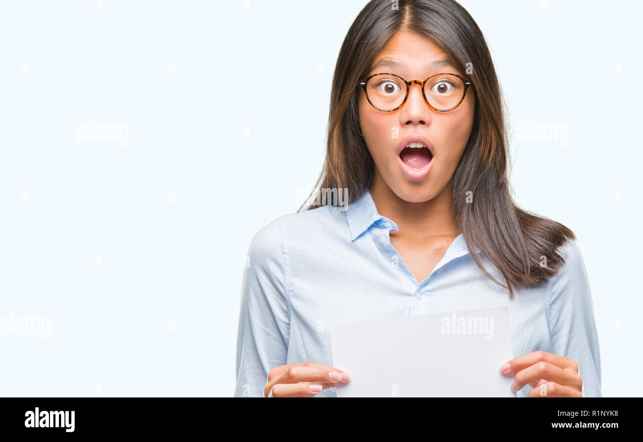Young asian woman over isolated background holding blank paper scared ...