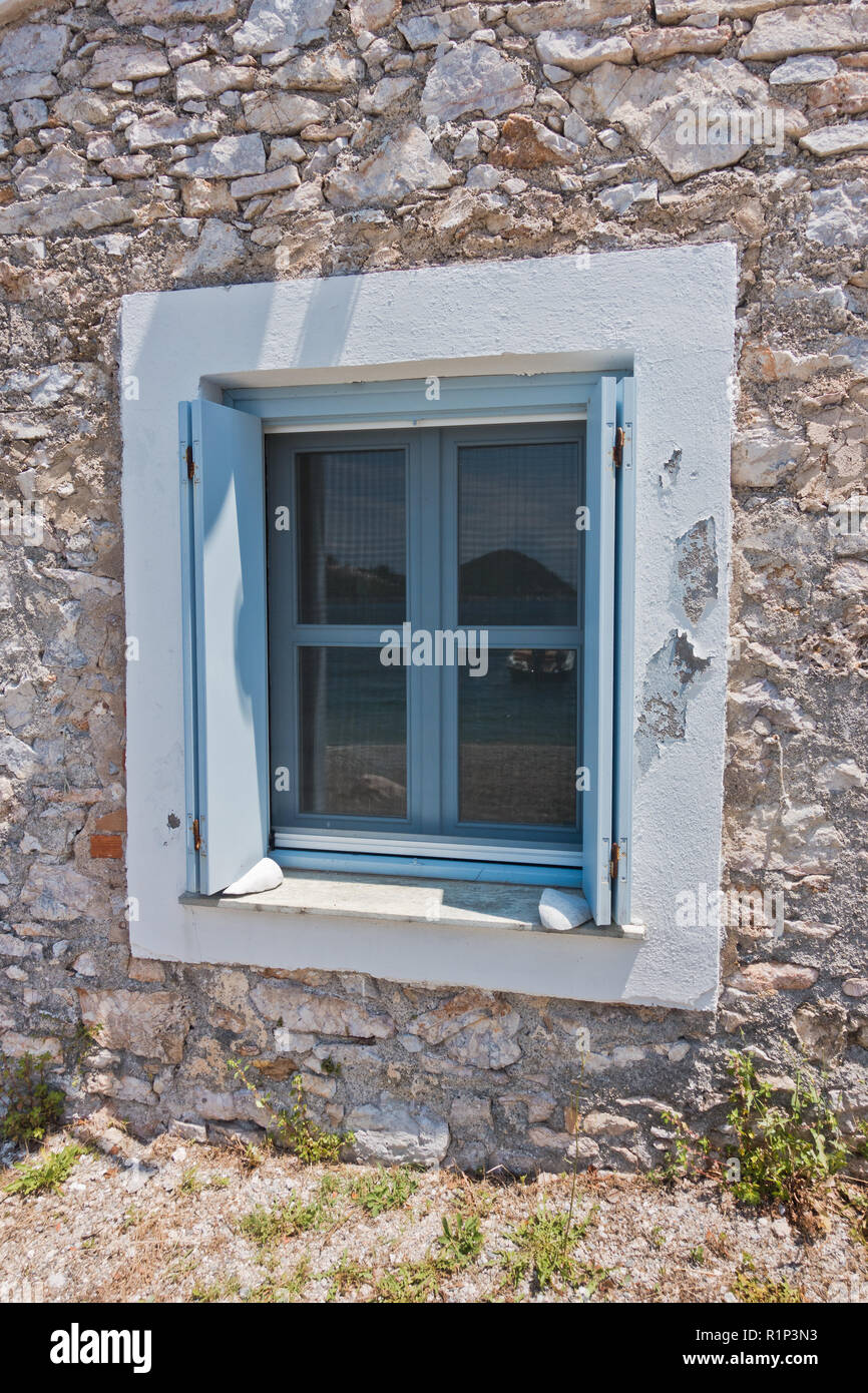 Blue and white window on an old greek house made of stone, Panormos bay ...