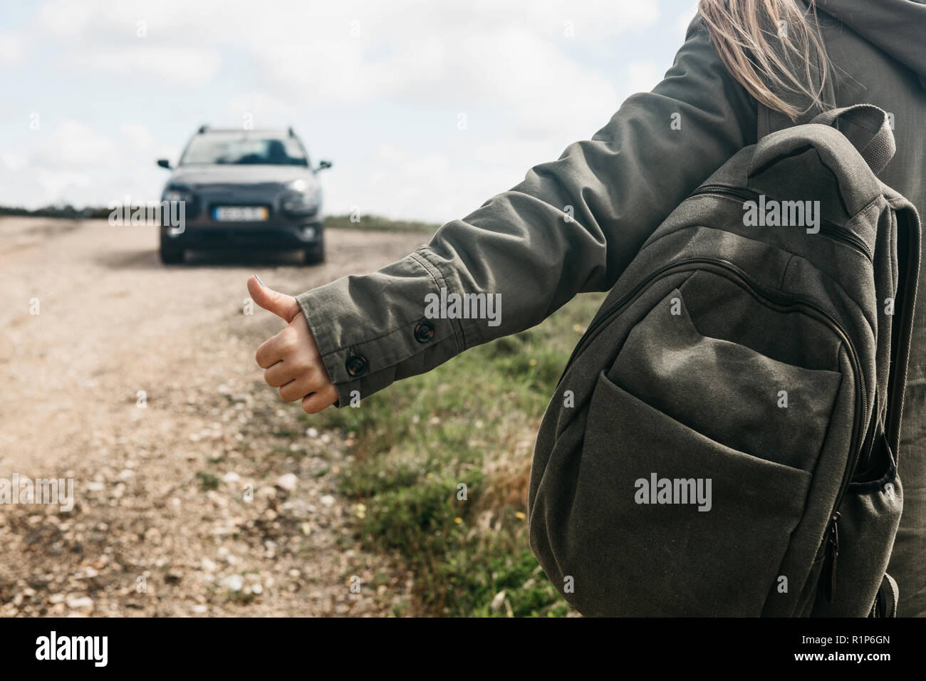 Close-up of a tourist girl with a backpack hitch-hiking. She raised her ...