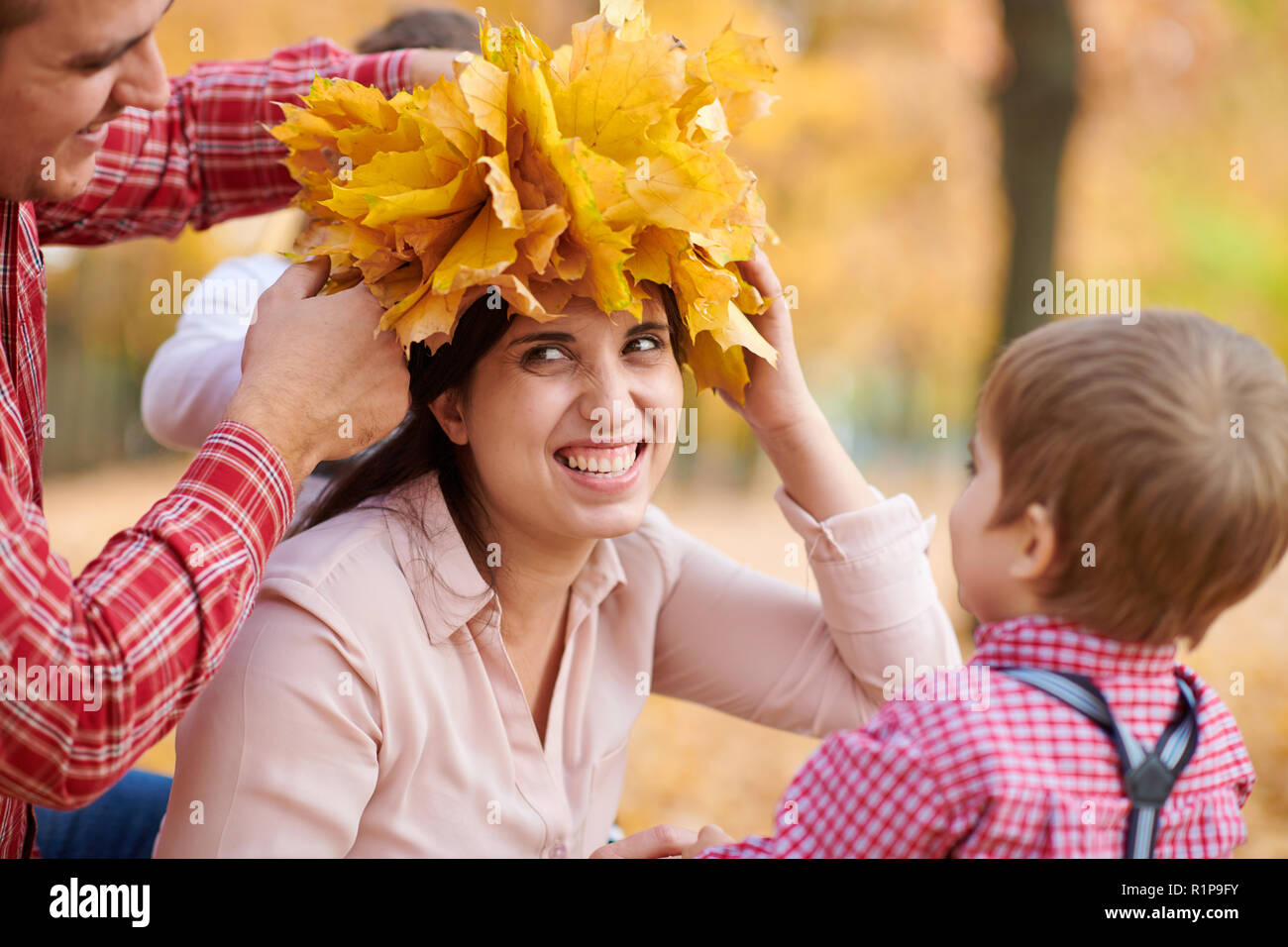 Father and son put yellow fallen leaves on mother head. Happy family is ...