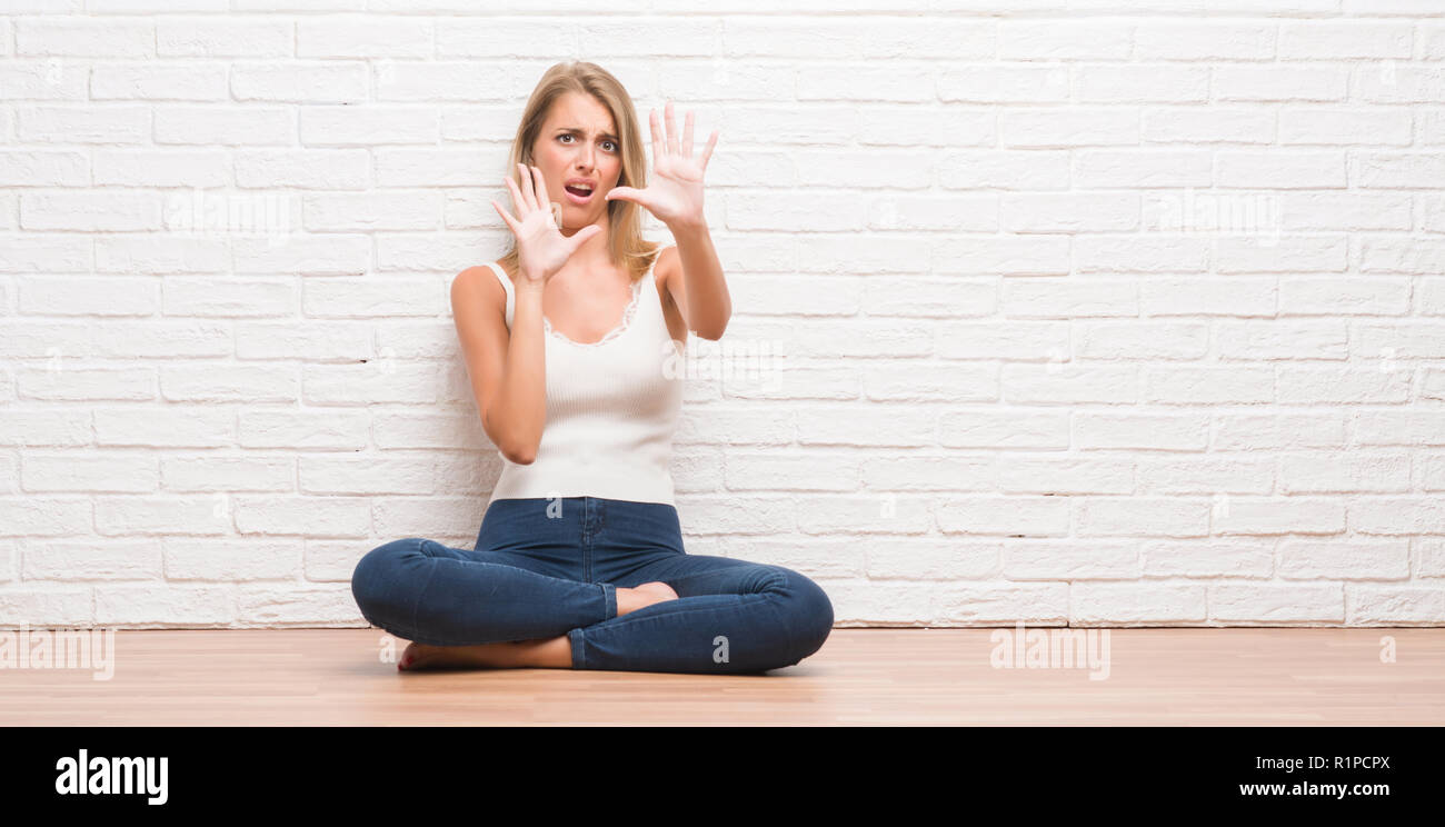 Beautiful young woman sitting on the floor at home afraid and terrified ...