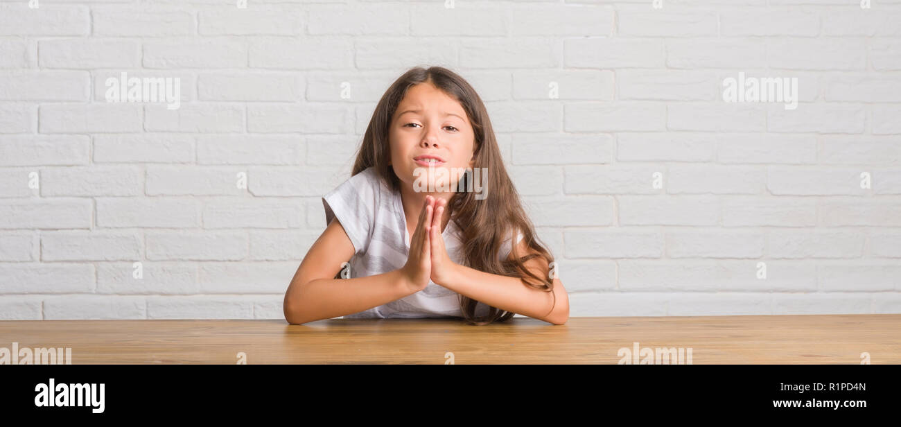 Young hispanic kid sitting on the table at home begging and praying ...