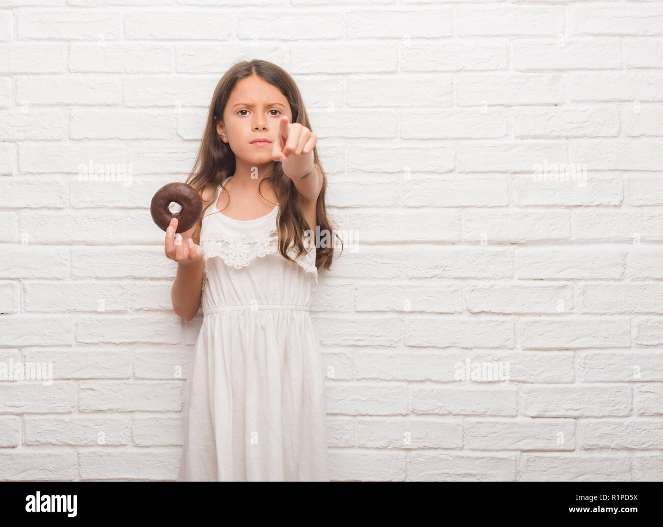 Young hispanic kid over white brick wall eating chocolate donut ...