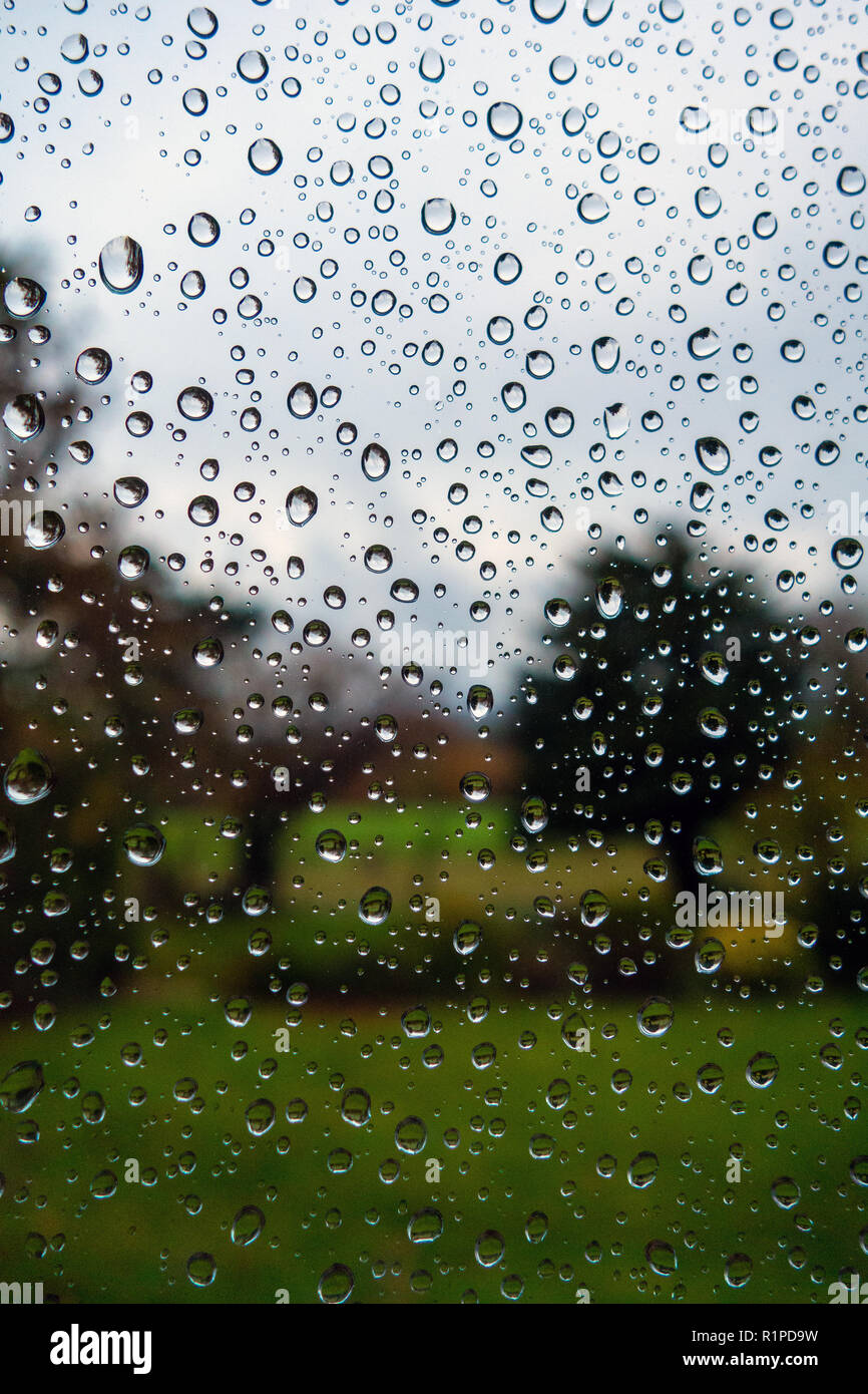 Raindrops on glass window against garden scene with bright sky, trees ...