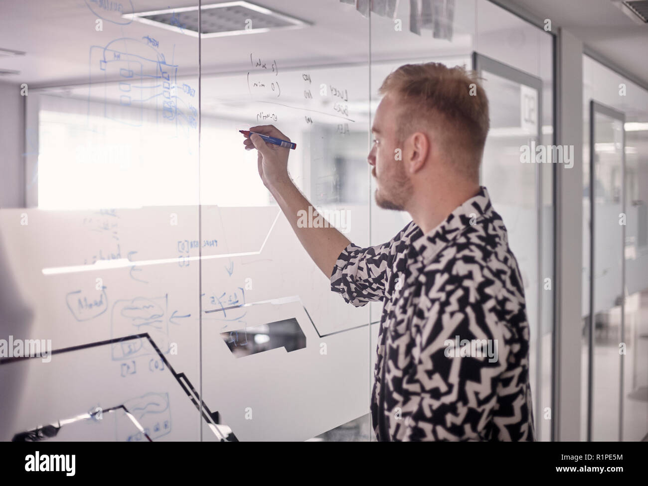 one young man, writing on glass window wall of modern office, with ...