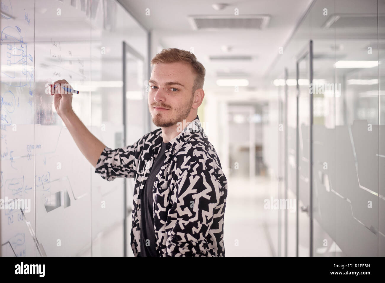 one young man, writing on glass window wall of modern office, with ...