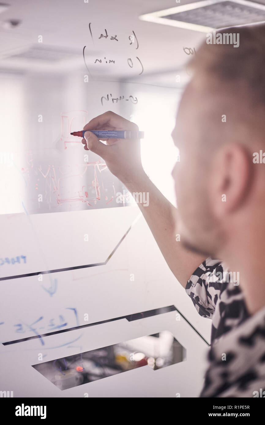 close-up one young man, writing on glass window wall of modern office ...