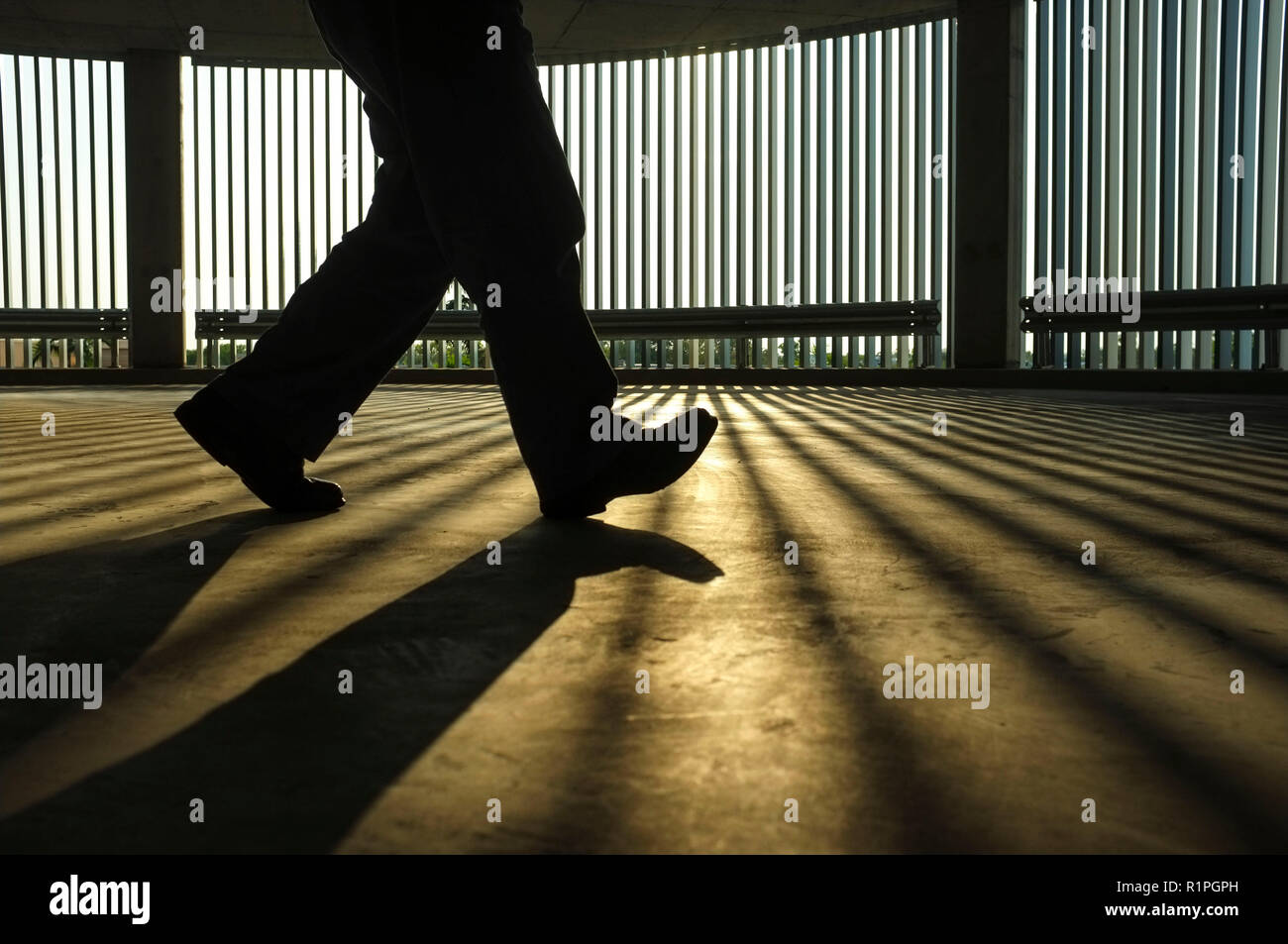 Backlighted low section of a man walking in the shadow of a car park ...