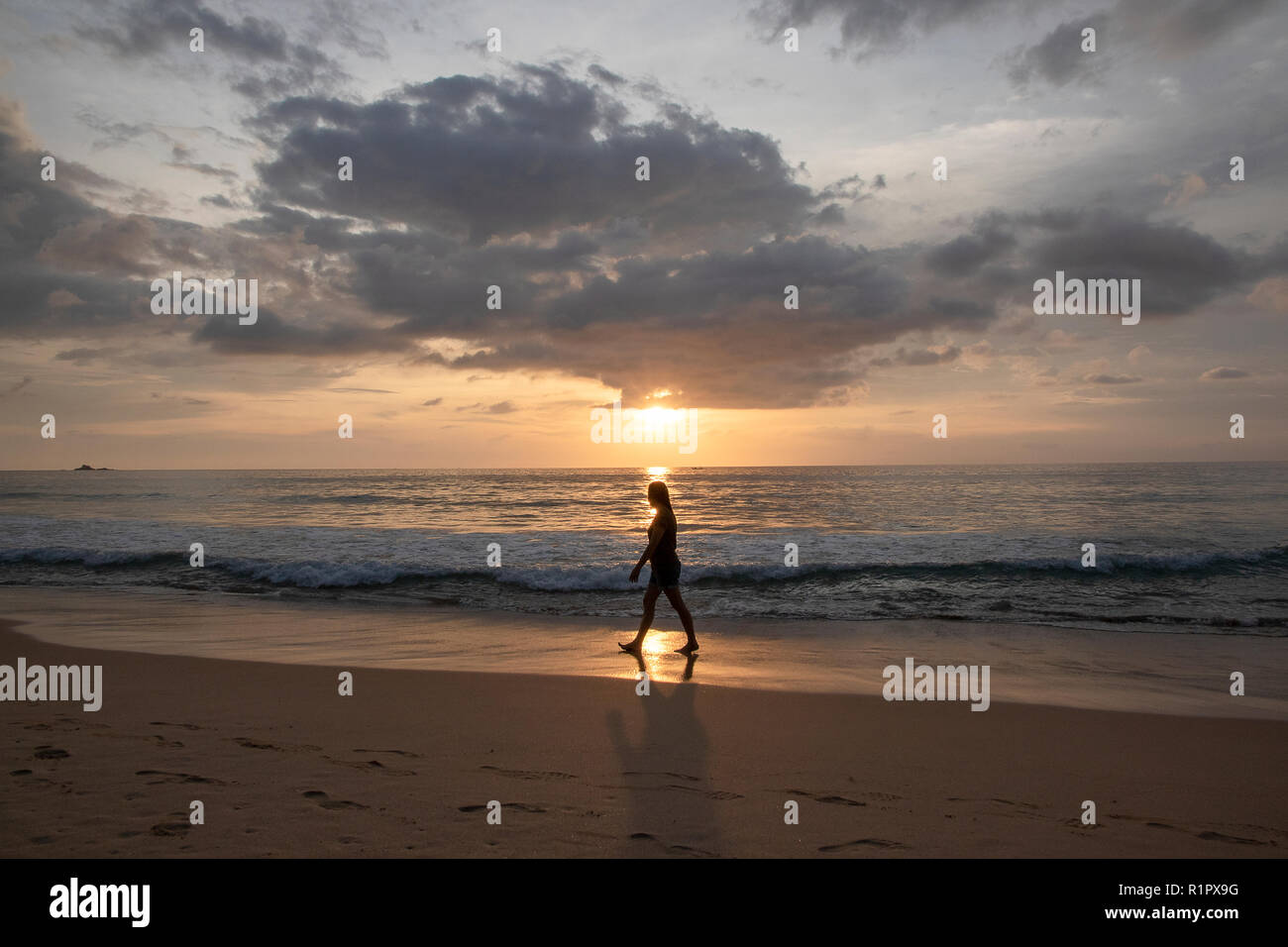 Woman walking at sunset on the sand beach Stock Photo - Alamy