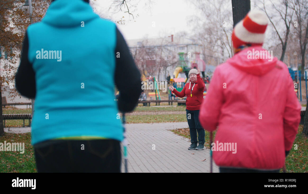 Elderly women walking on sticks of nordic walking on a sidewalk. Back ...
