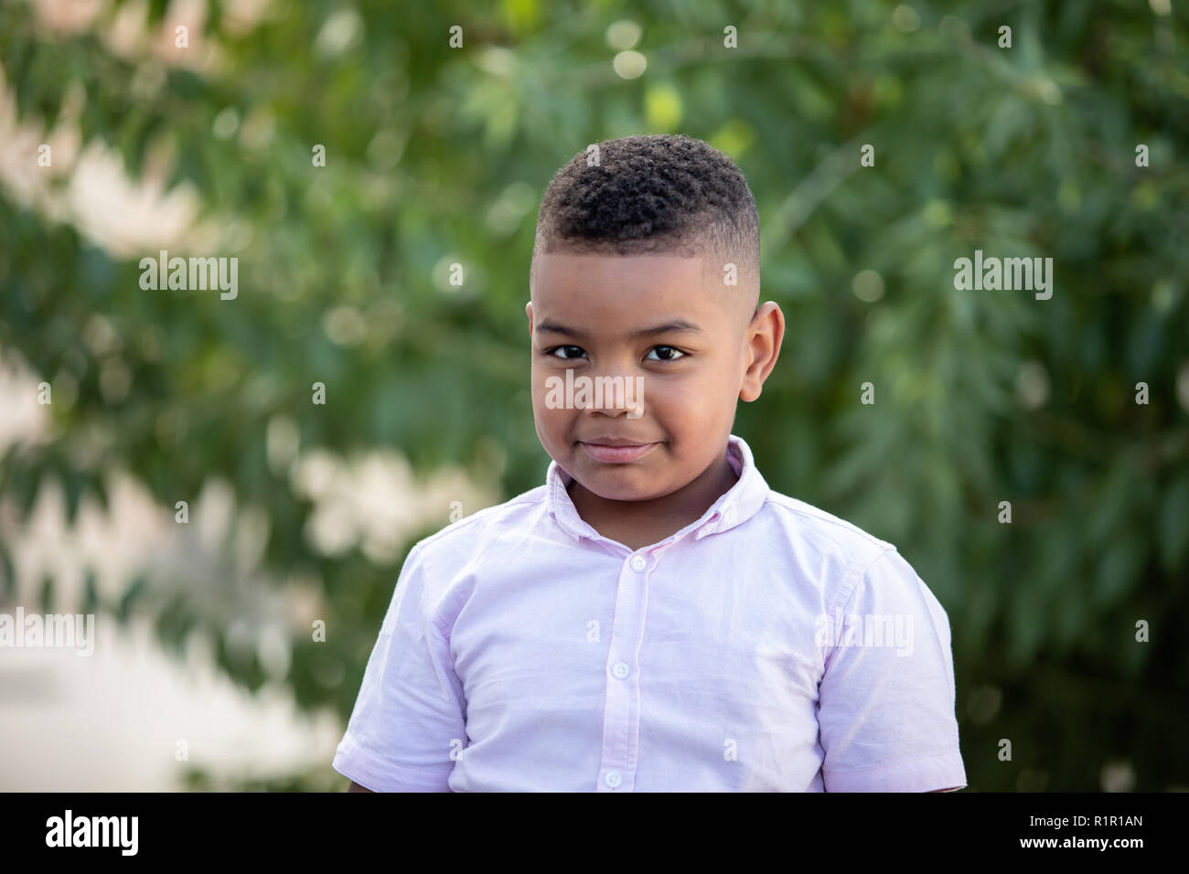 Adorable latin child in the garden with a beautiful green of background ...