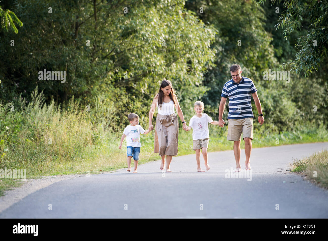 A family with two small sons walking barefoot on a road in park on a ...