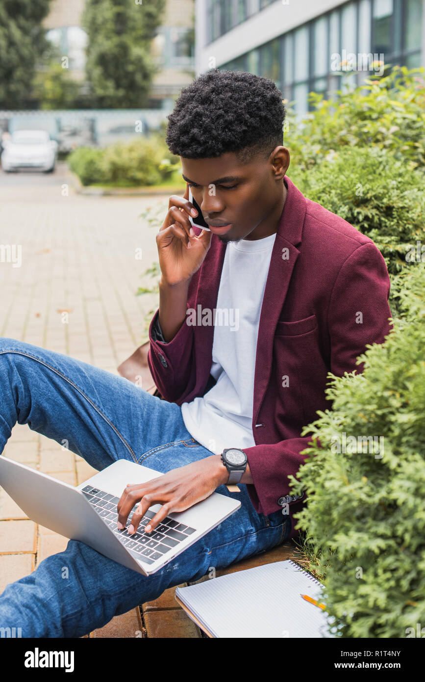 young freelancer using laptop and writing in notebook while sitting on ...