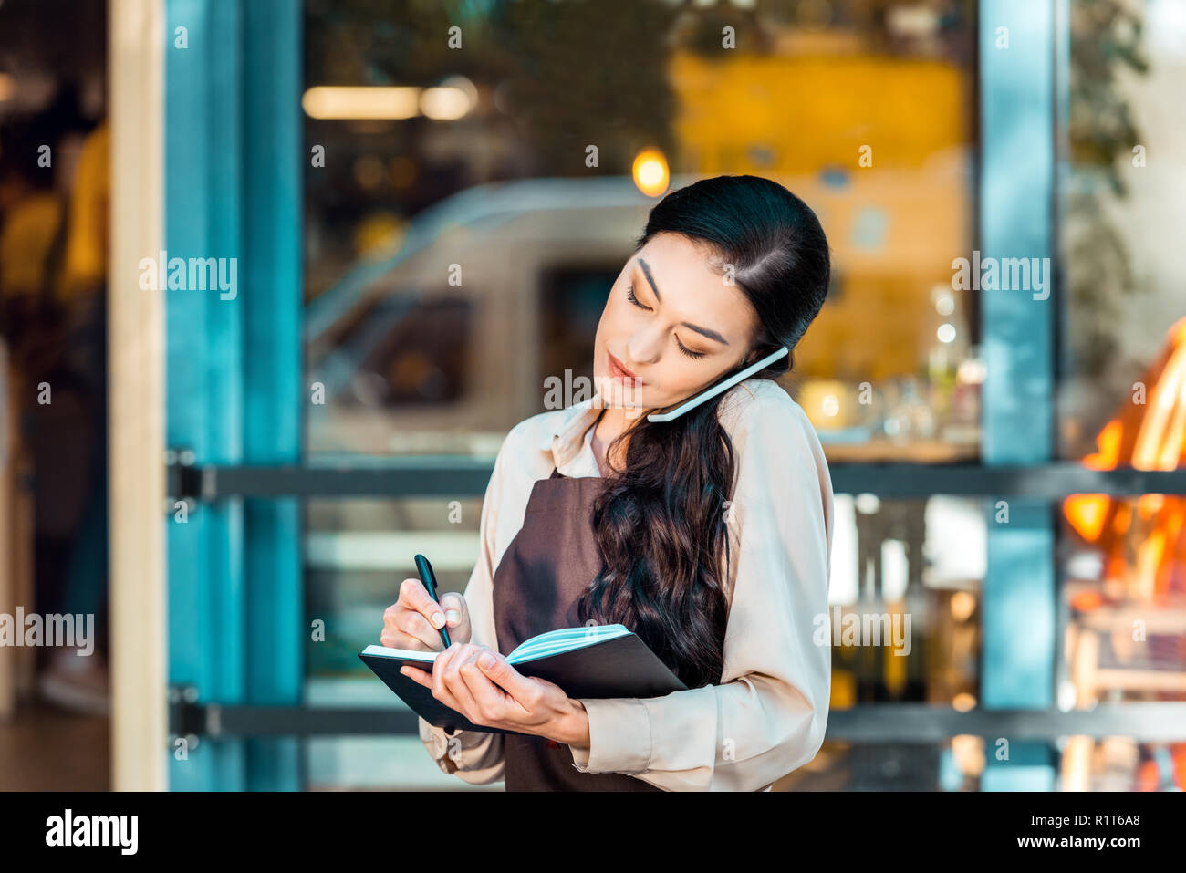 attractive waitress talking by smartphone on street near cafe and ...