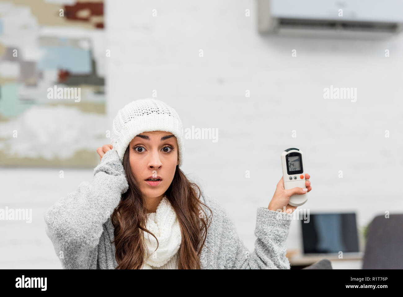 shocked young woman in warm clothes holding air conditioner remote ...