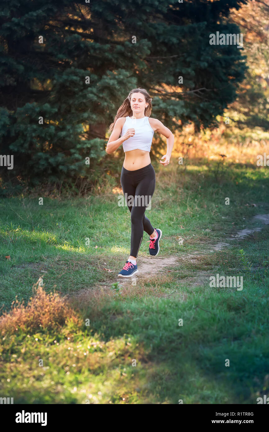 Beautiful young sportive woman jogging in the park in sunset light ...