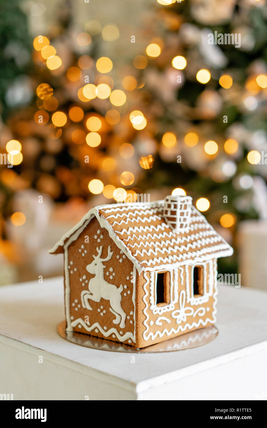 Gingerbread house on table. Defocused lights of Christmas tree. Morning ...