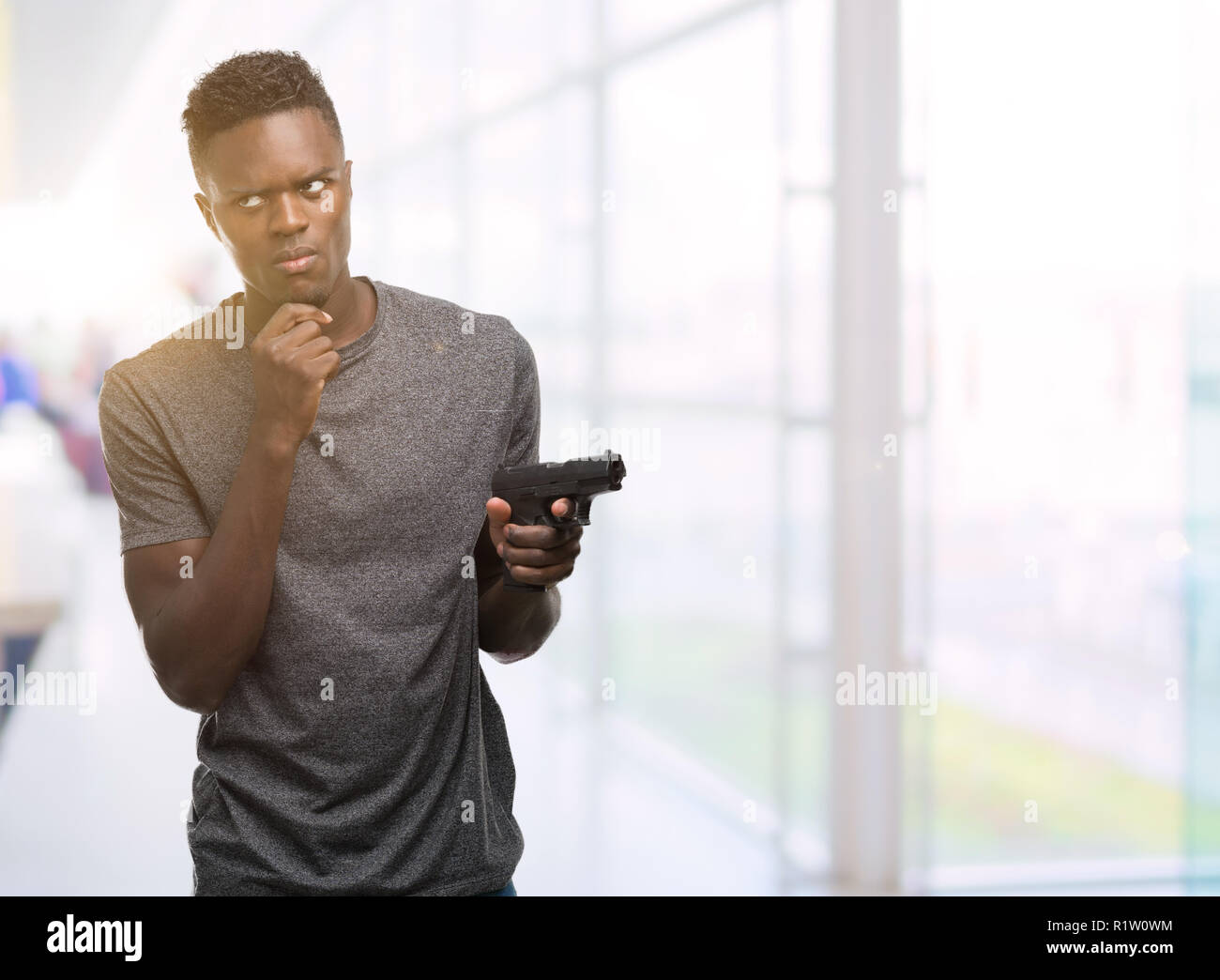 Young african american man holding a gun serious face thinking about ...