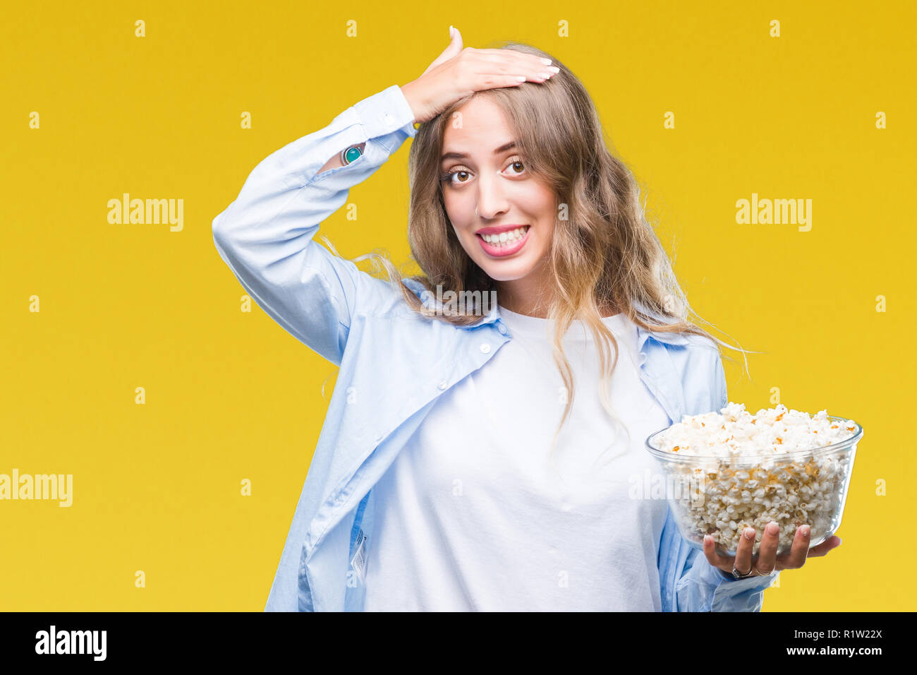 Beautiful young blonde woman eating popcorn over isolated background ...