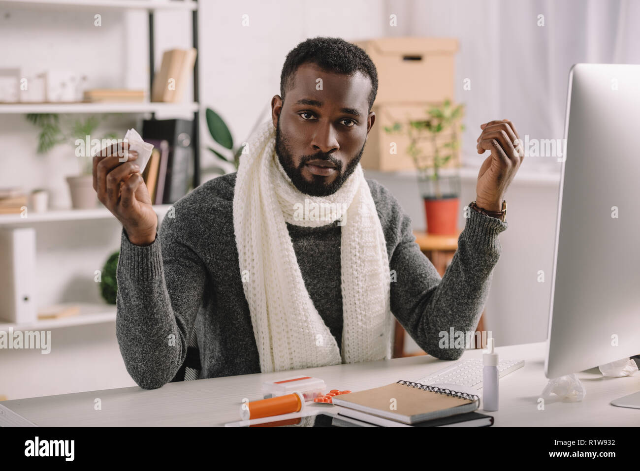 diseased african american man holding napkin while sitting at workplace ...