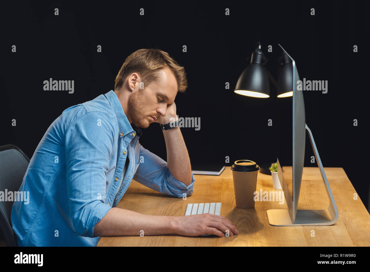 side view of businessman sleeping at table with computer and paper ...