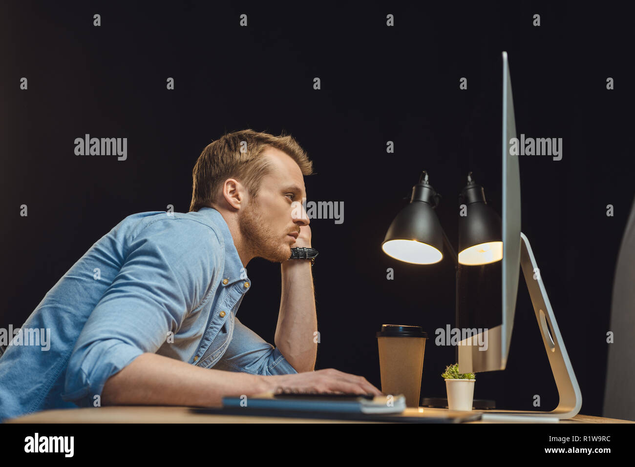 side view of overworked young businessman sitting at table with ...