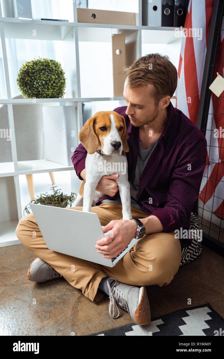 male freelancer with laptop holding beagle near usa flag in home office ...