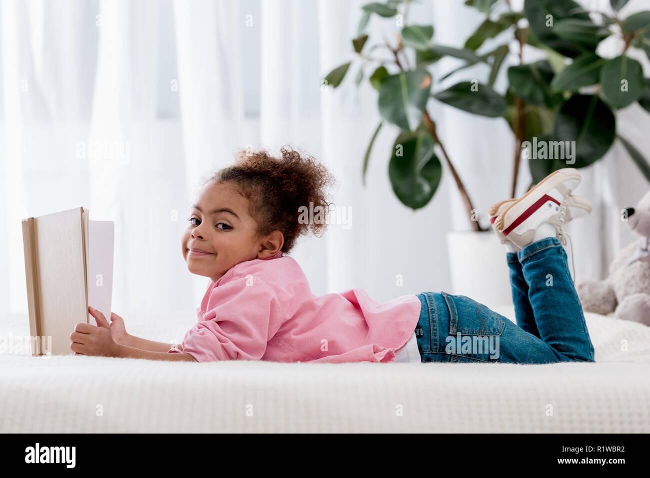 Side view of adorable African american child laying on the bed and ...
