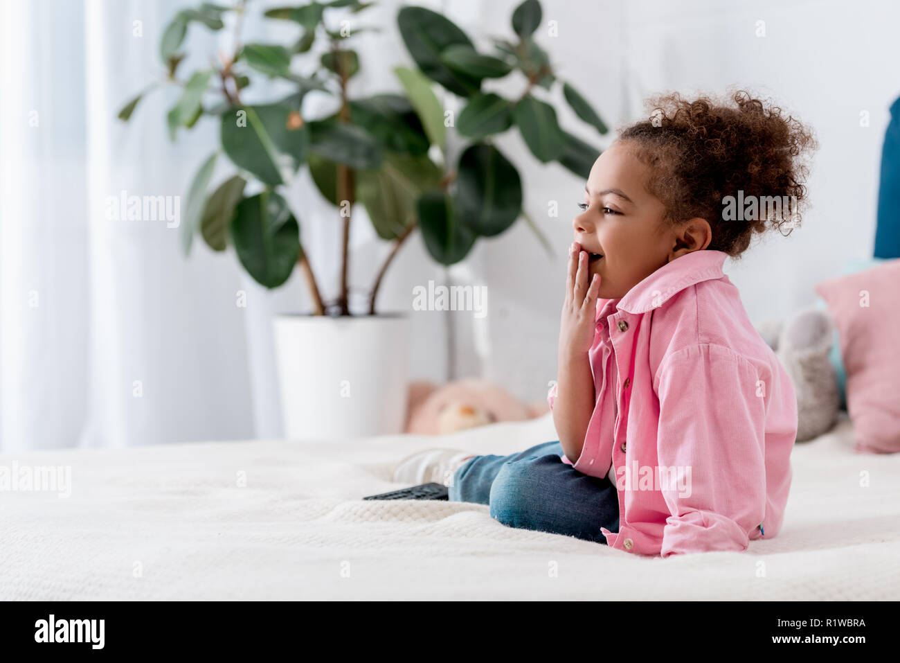 Cute yawning African american kid sitting on the bed Stock Photo - Alamy