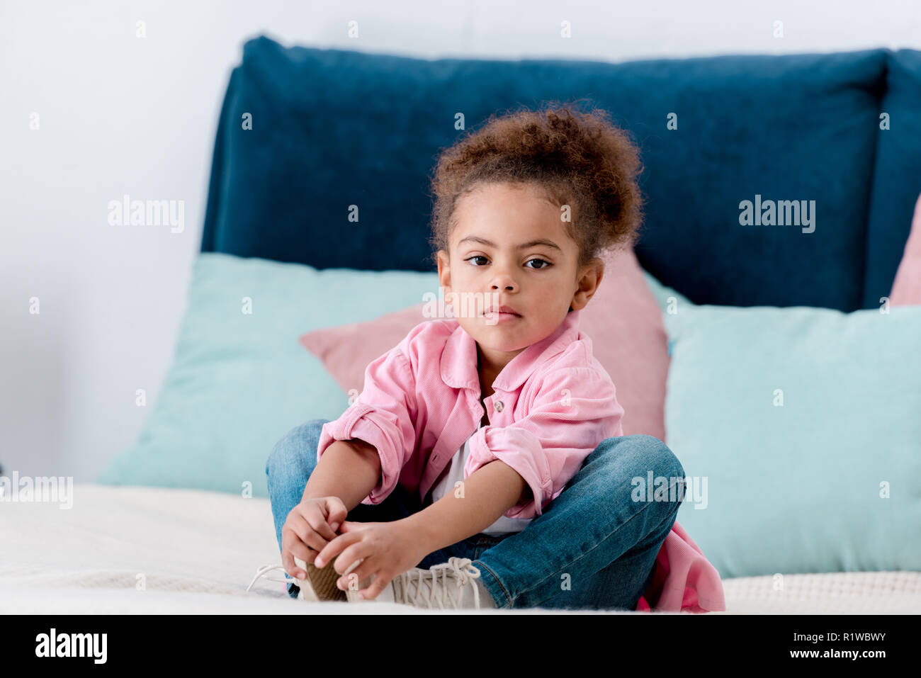 Cute african american child sitting on the bed clasping her legs Stock ...