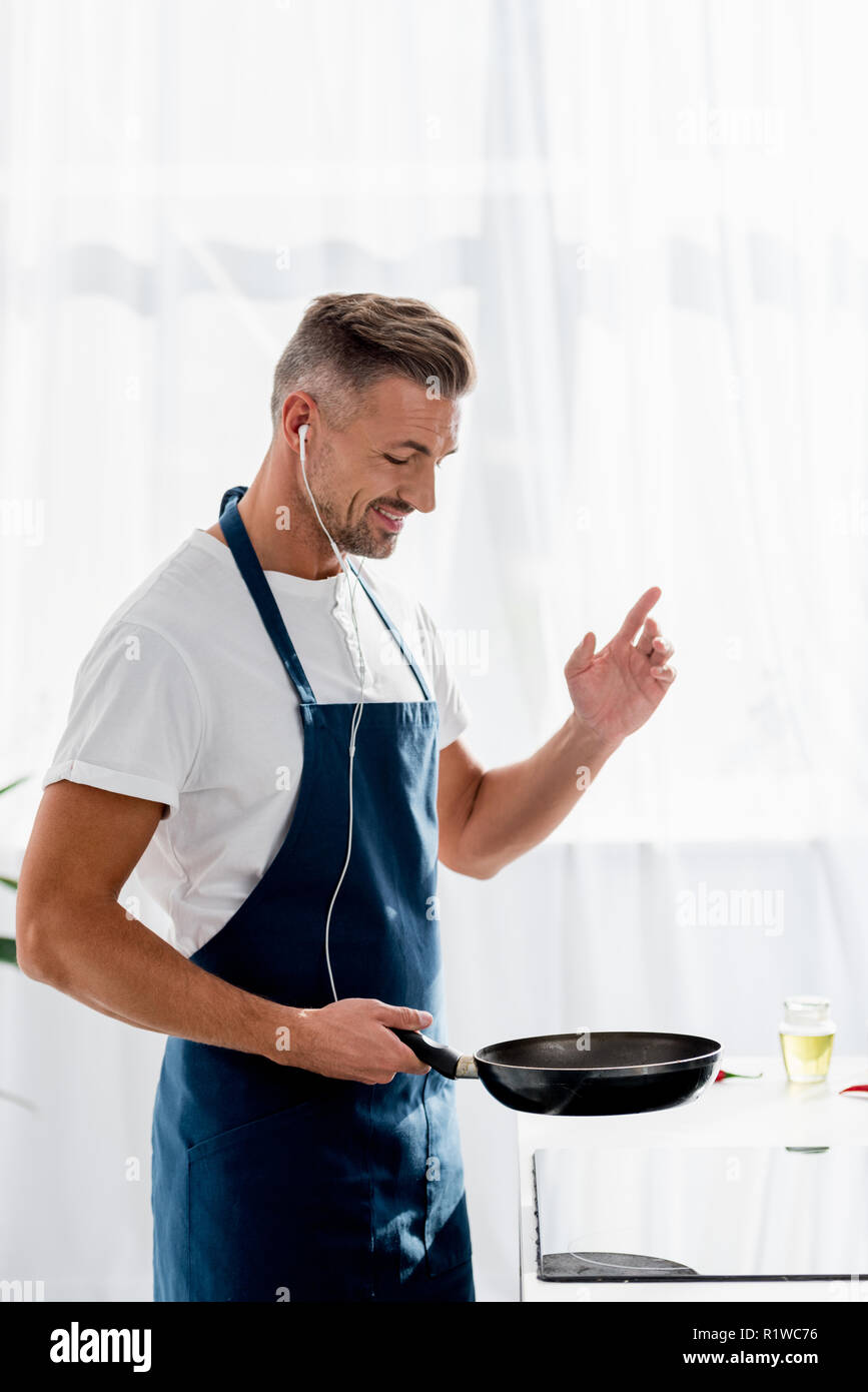 smiling man with earphones and pan in hand listening to music at ...