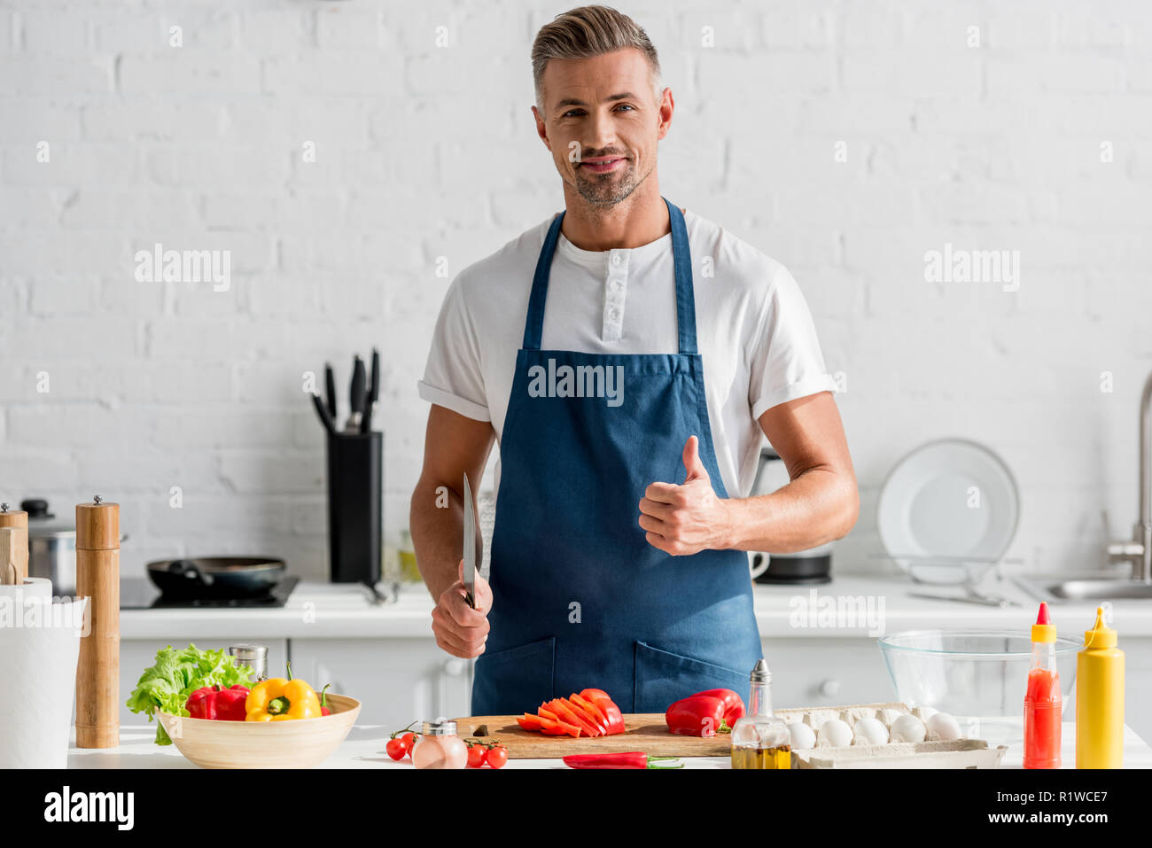man showing thumbs up with knife in hand standing at kitchen Stock ...