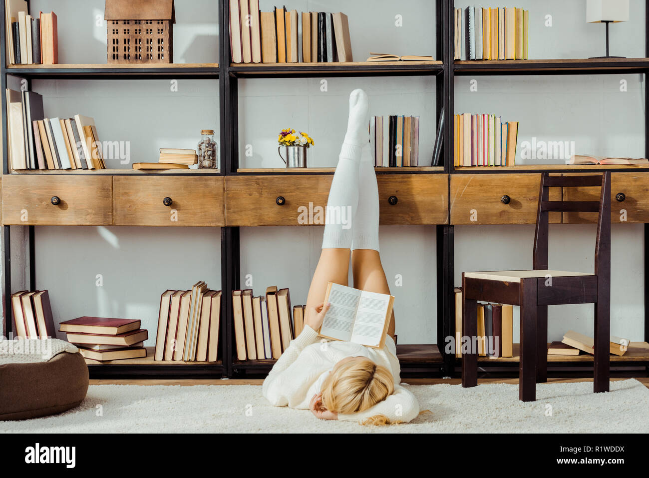 woman laying on carpet and reading book with legs on rack Stock Photo ...