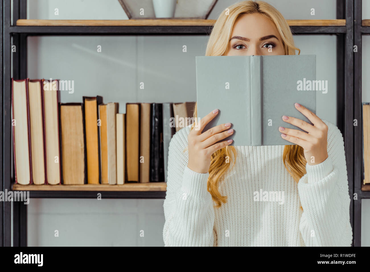 close up of blonde woman hiding face behind book Stock Photo - Alamy