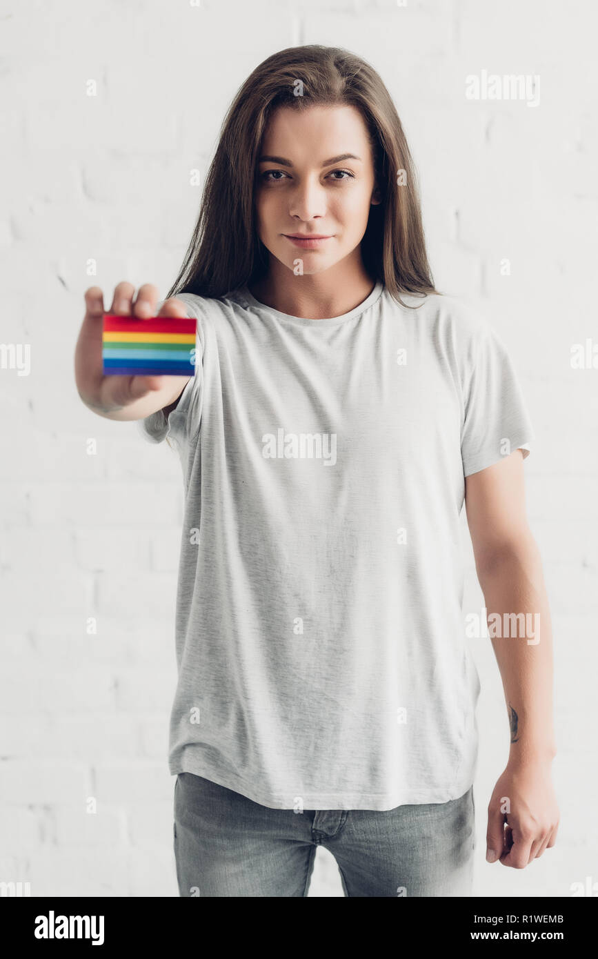 young transgender man holding card with pride flag in front of white ...