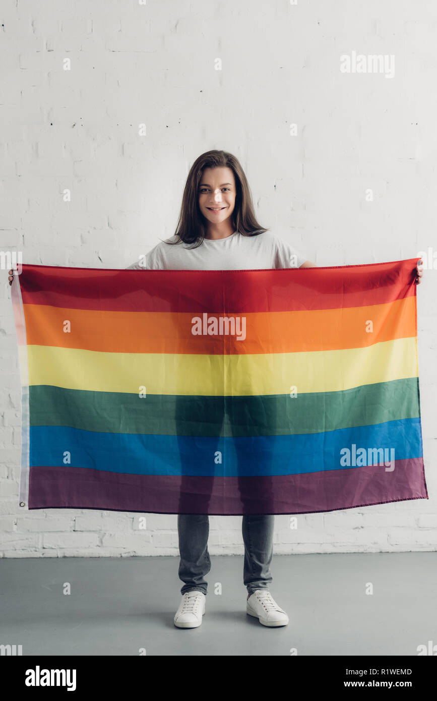 happy transgender man holding pride flag in front of white brick wall ...