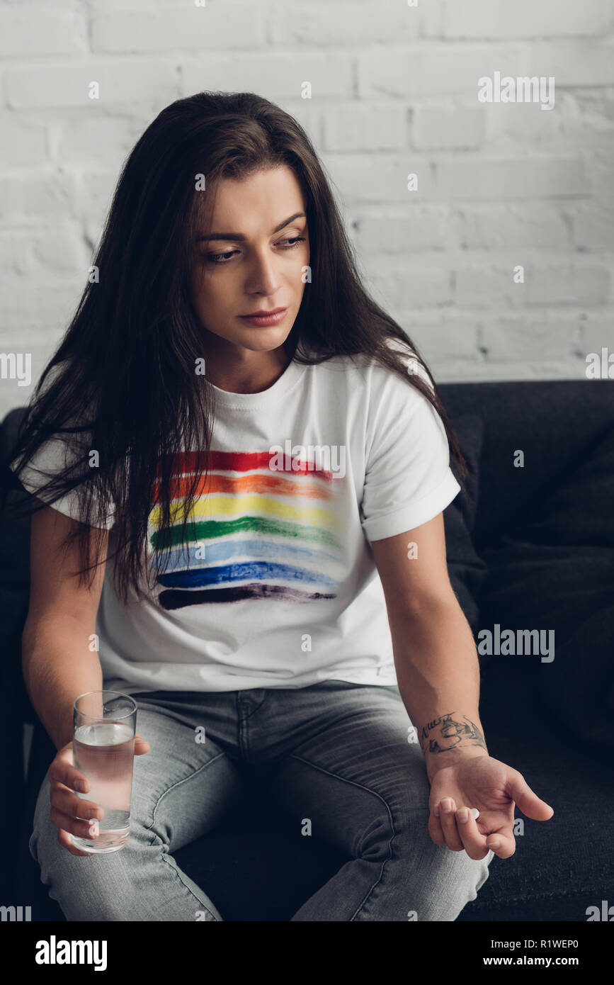 depressed young transgender man with pill and glass of water sitting on ...