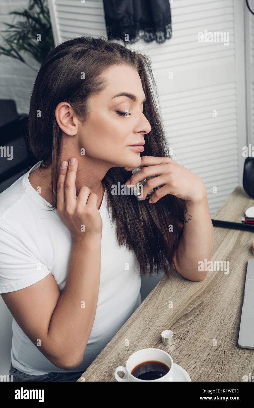 close-up portrait of young transgender man applying perfume on neck at ...