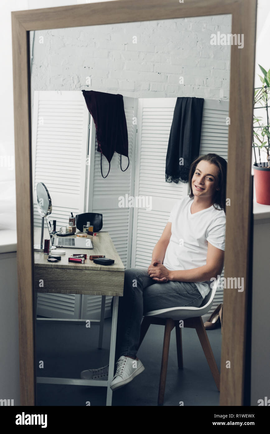 view through mirror reflection young transgender man looking at camera ...