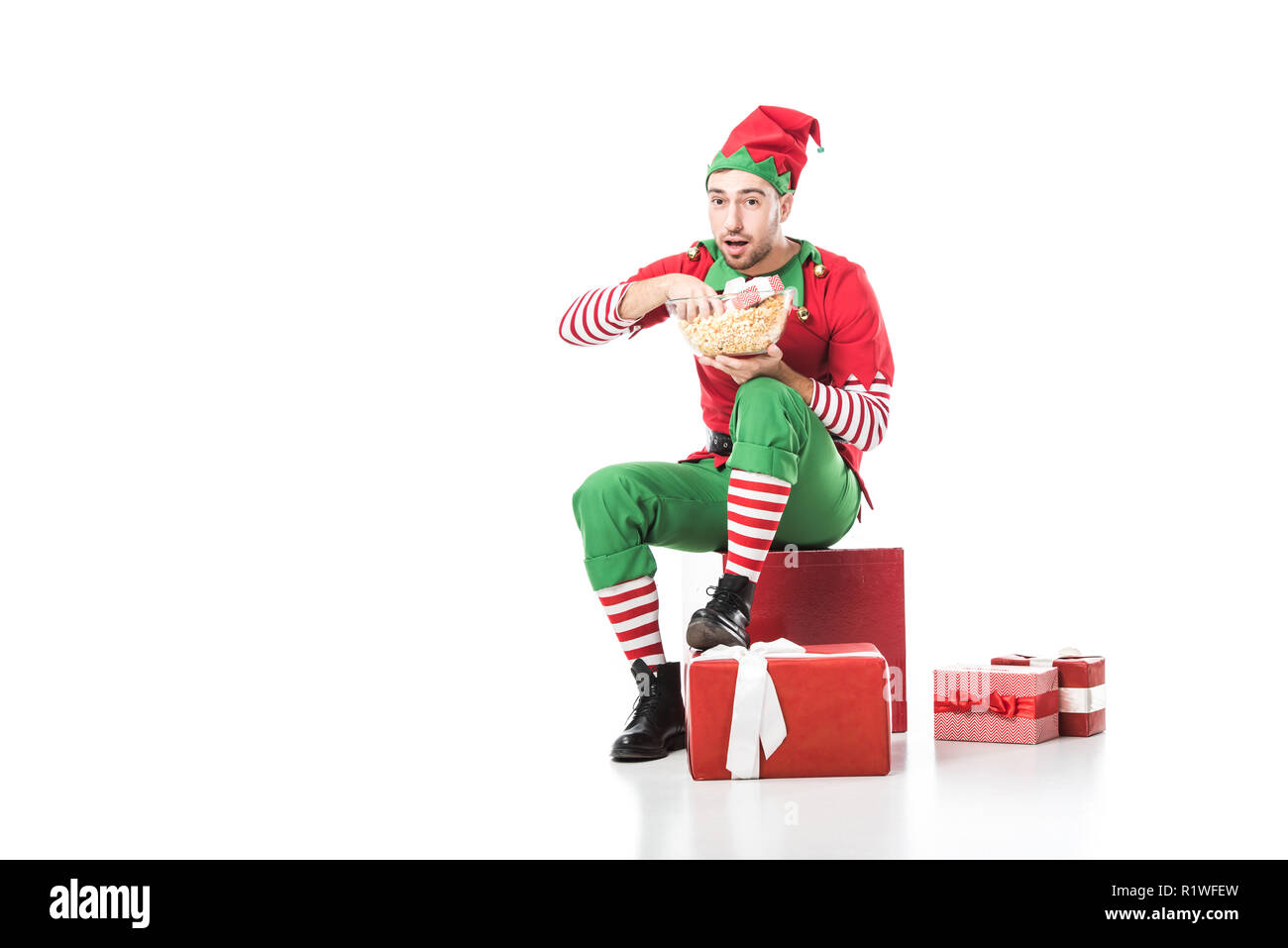 man in christmas elf costume sitting on pile of presents and eating ...