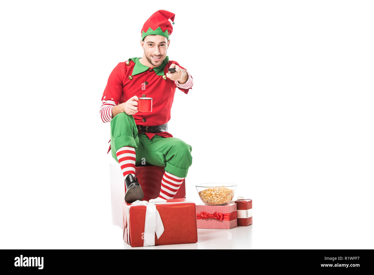 man in christmas elf costume sitting on pile of presents, holding cup ...