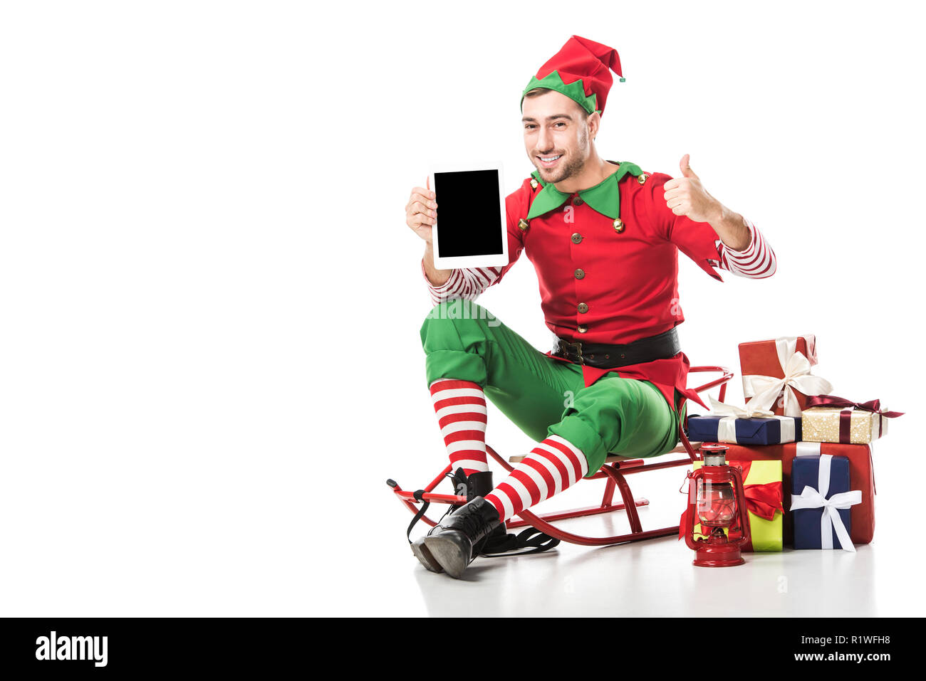 man in christmas elf costume sitting on sleigh and holding tablet with ...