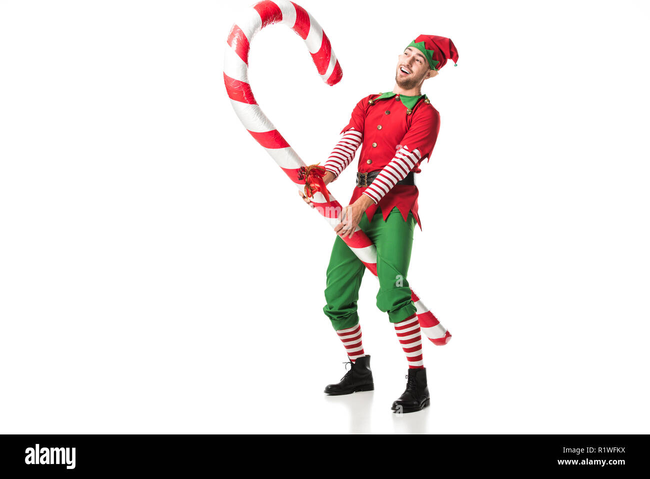 cheerful man in christmas elf costume riding big candy cane isolated on ...