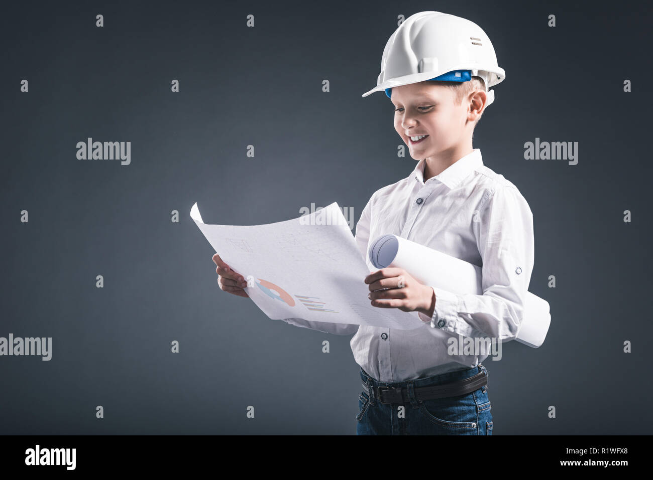 portrait of smiling boy in architect helmet looking at blueprints in ...
