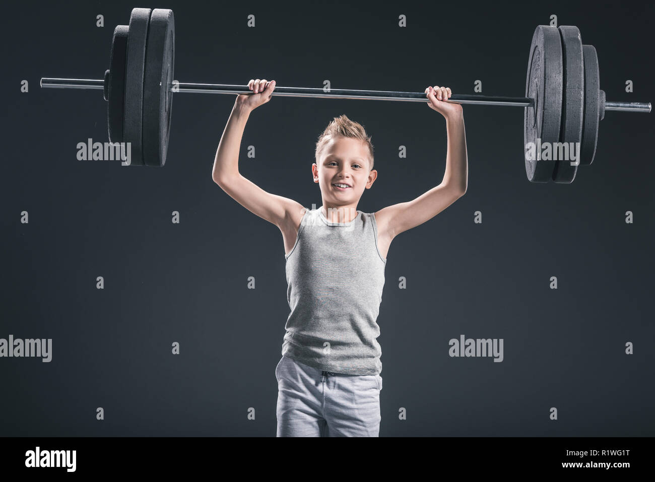 portrait of pre-adolescent boy in sportswear holding barbell on dark ...