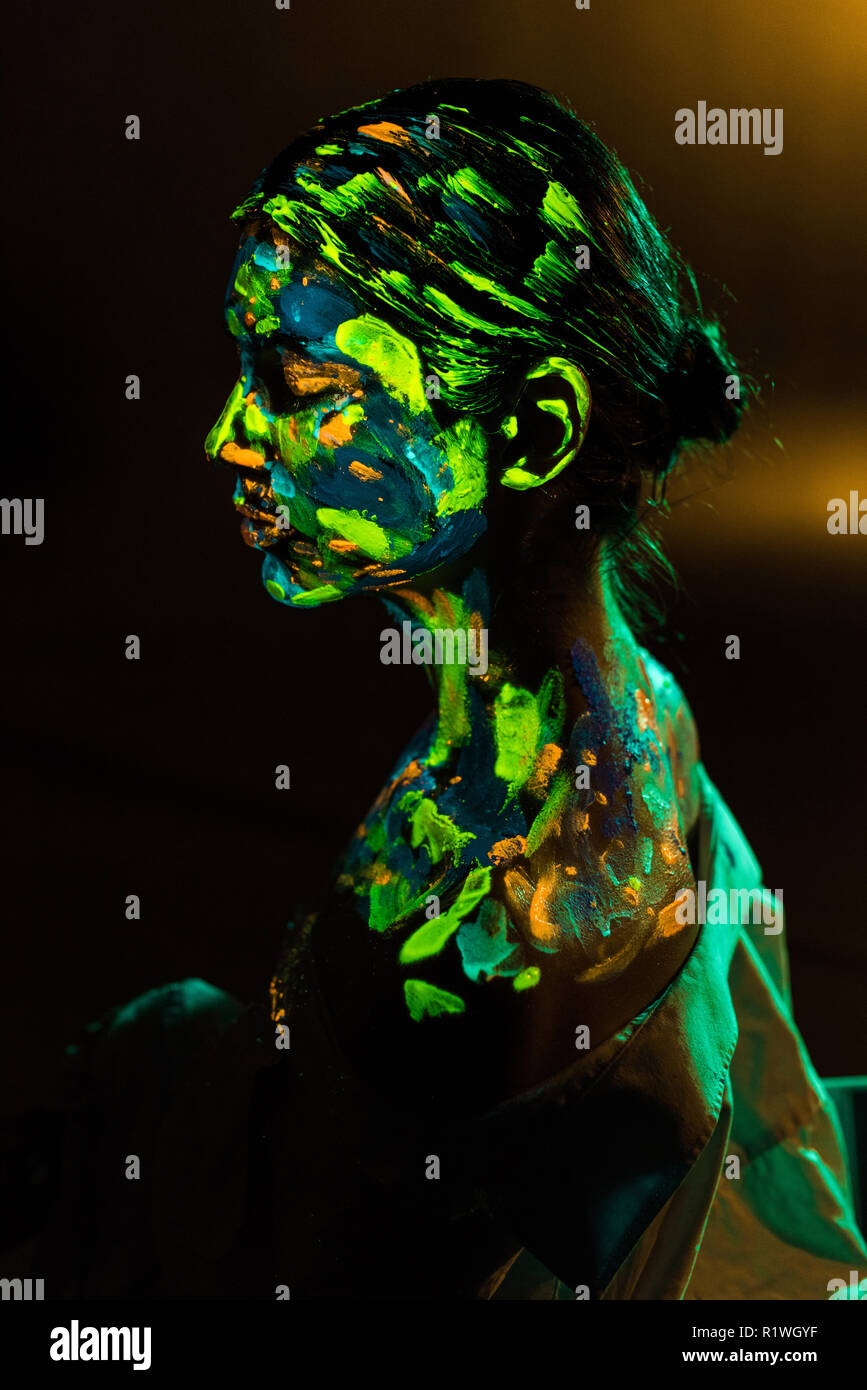 side view of woman painted with colorful ultraviolet paints on black ...