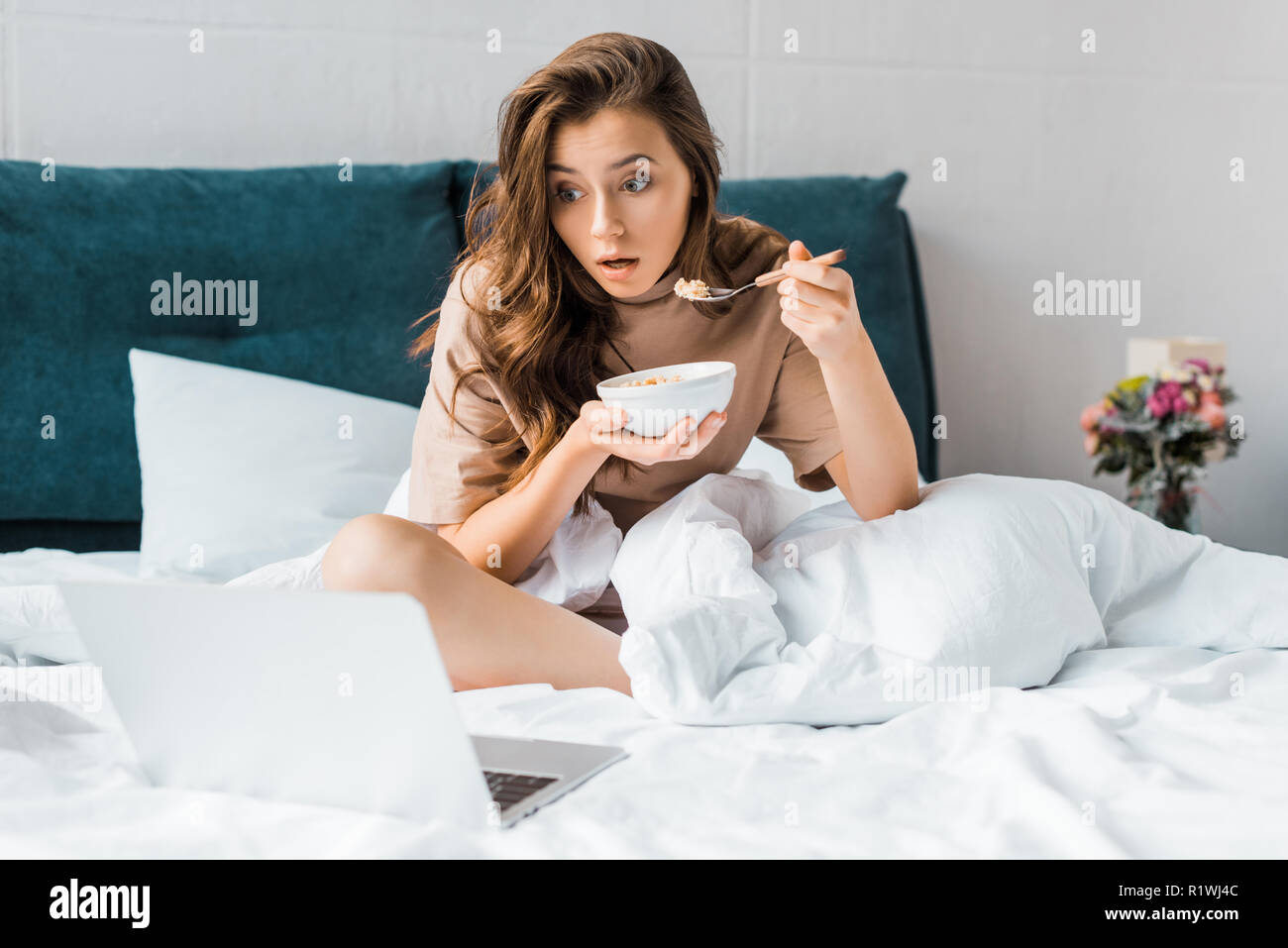 Shocked Brunette Girl With Bowl Of Oatmeal Watching Something On Laptop 6412