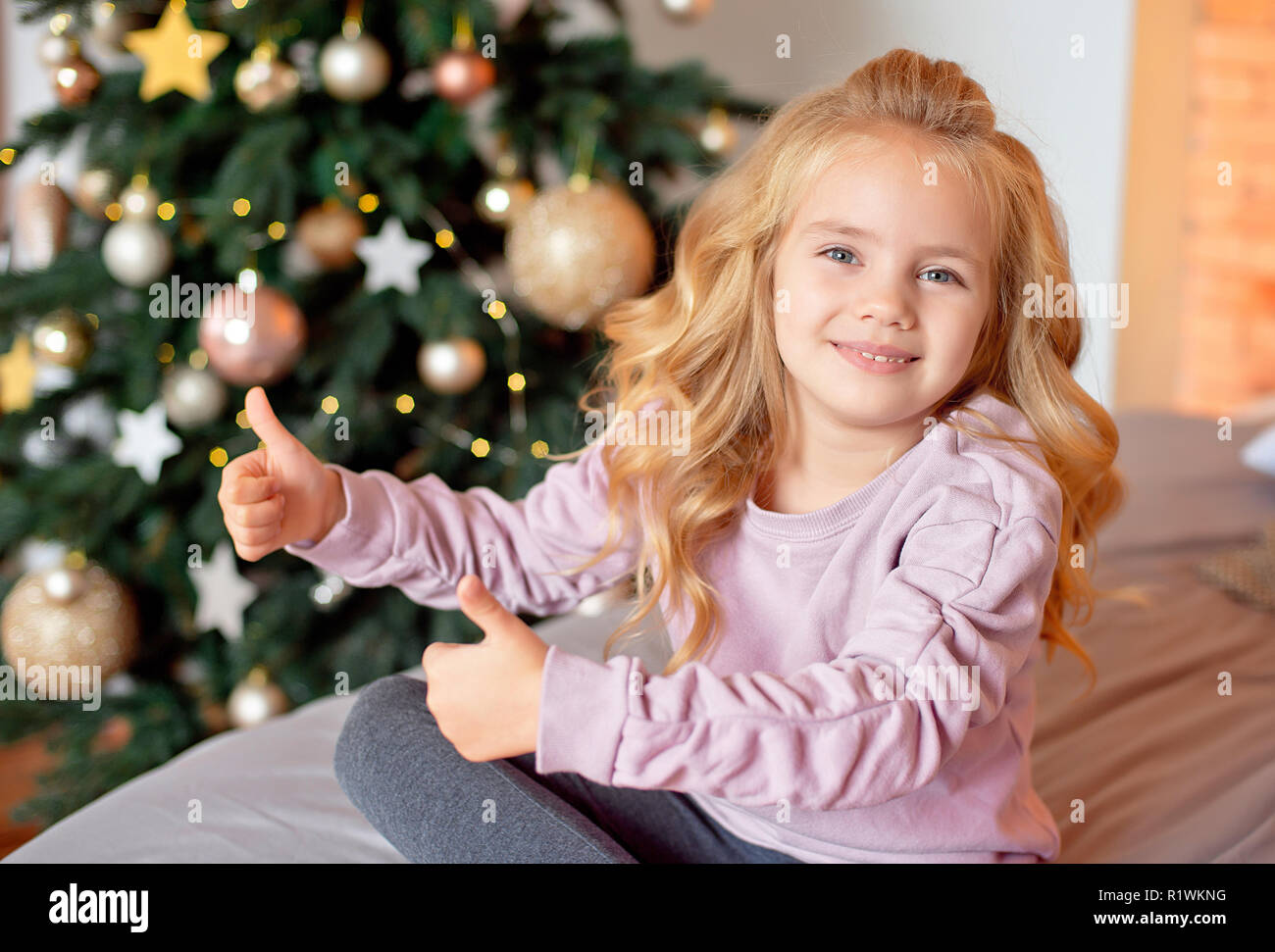 Cute pretty little girl with a beaming smile lying on her stomach a bed ...