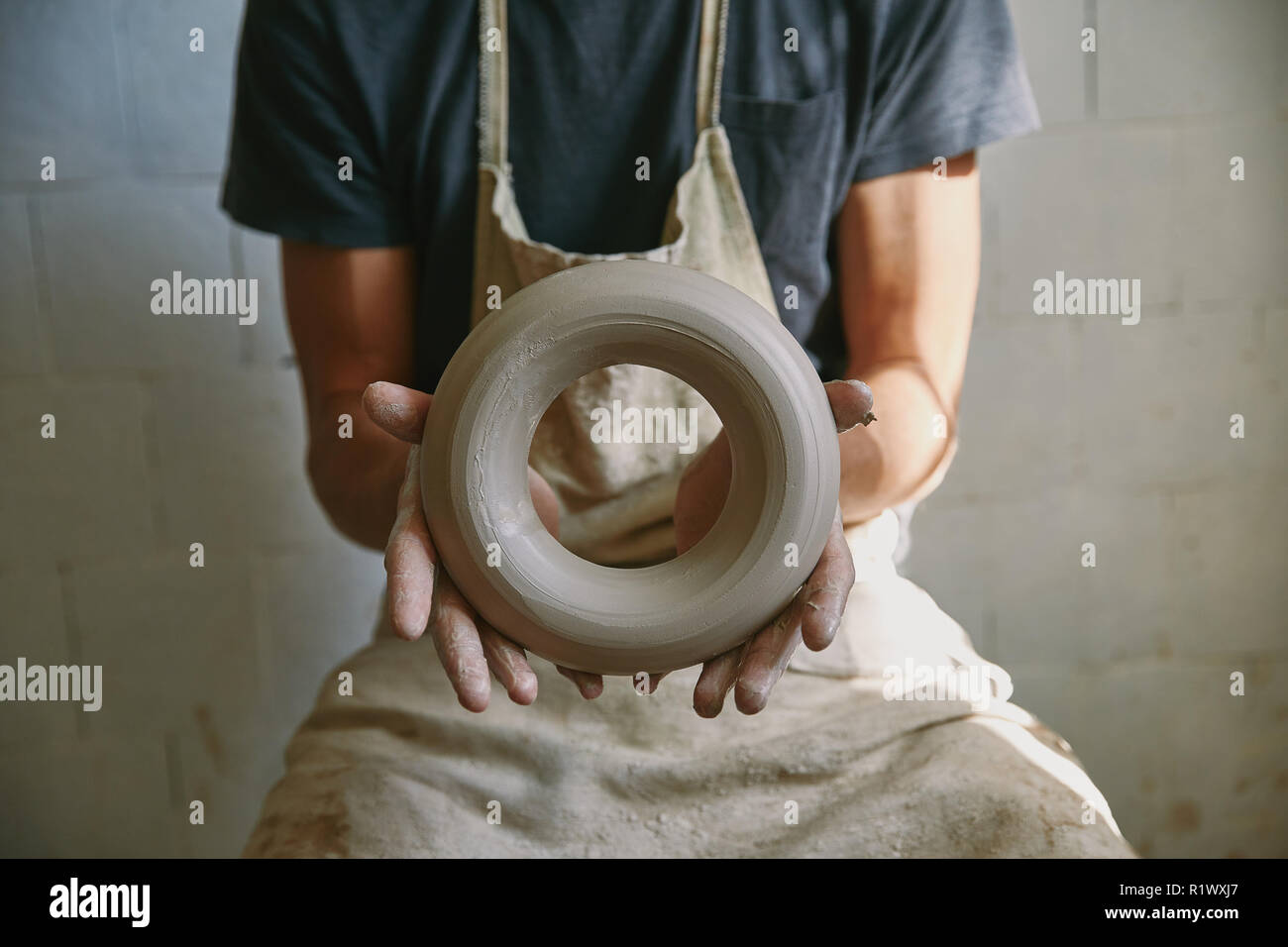 selective focus of professional potter in apron holding clay at pottery ...