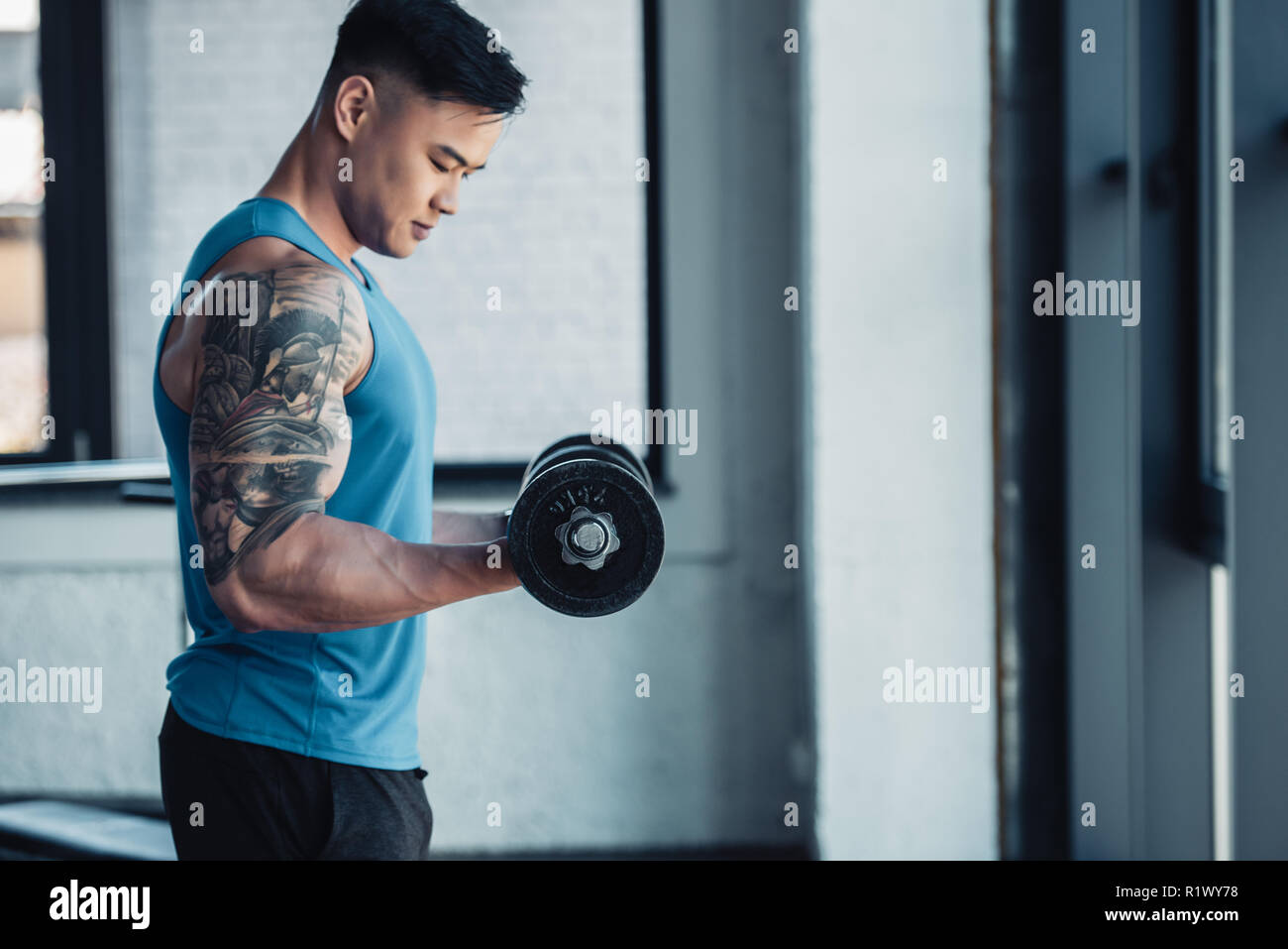 concentrated side view of young sportsman exercising with dumbbell in ...